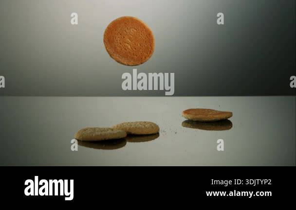 Round golden brown cookies falling and bouncing on a dark reflective ...