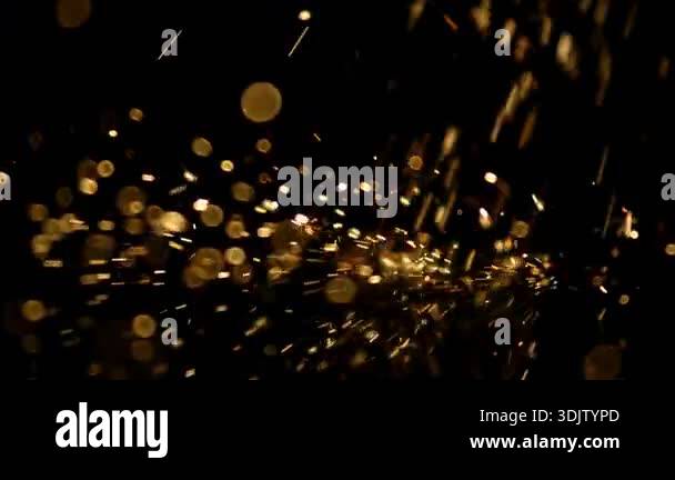 Intense shower of bright golden sparks flying across a dark background ...