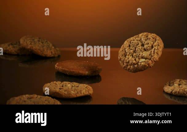 Round baked oatmeal cookies falling and rolling across a dark ...