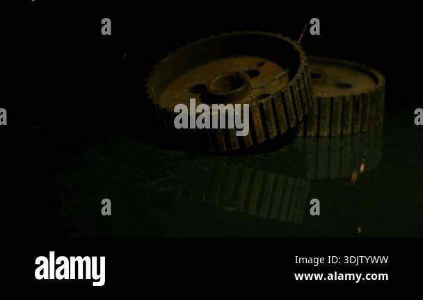 Two old rusty metal cogs and gears lying on a dark reflective surface ...