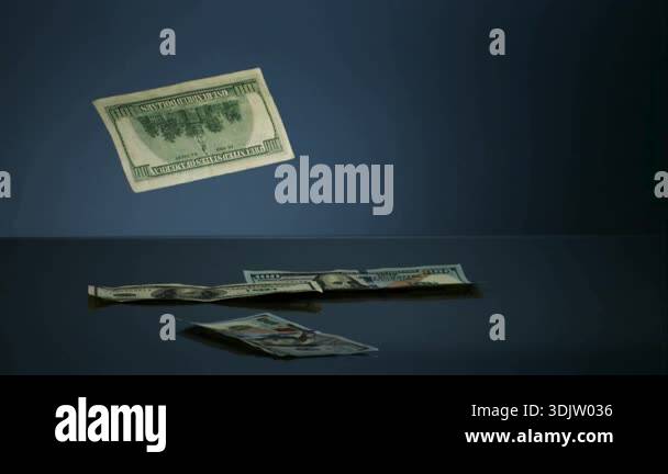 Several one hundred dollar bills falling slowly and settling on a dark ...