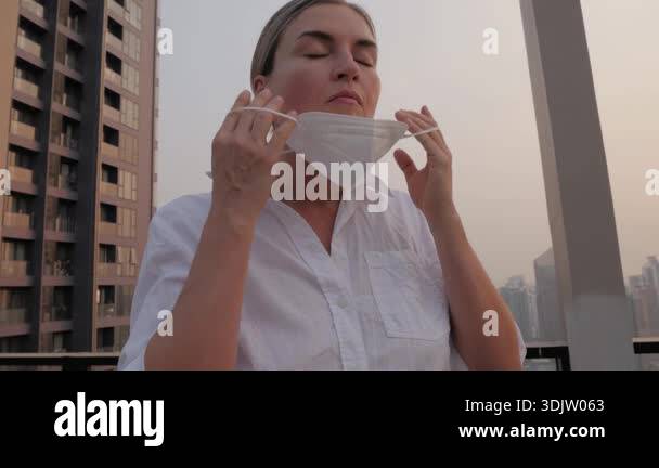 Woman removing face mask and breathing fresh air on rooftop, relief ...