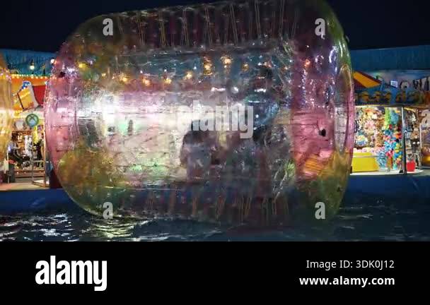 Children playing inside an inflatable water roller at a nighttime ...