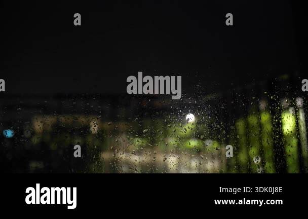 Close up of raindrops on glass with blurred lightning flashes on ...