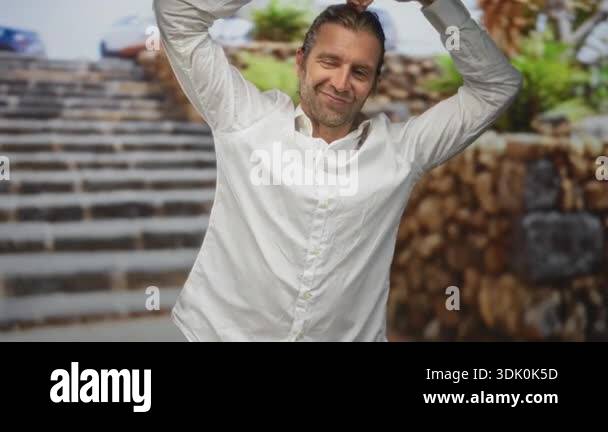 Man wearing white shirt makes heart shape gesture with hands on street ...