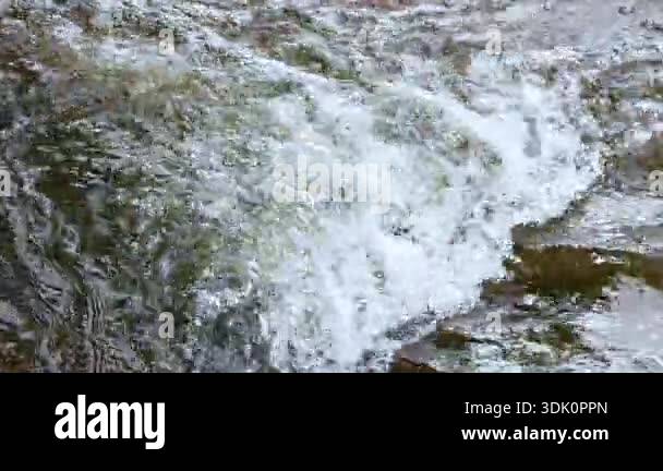 A dynamic stream flows over mossy rocks, creating bubbles and splashes ...