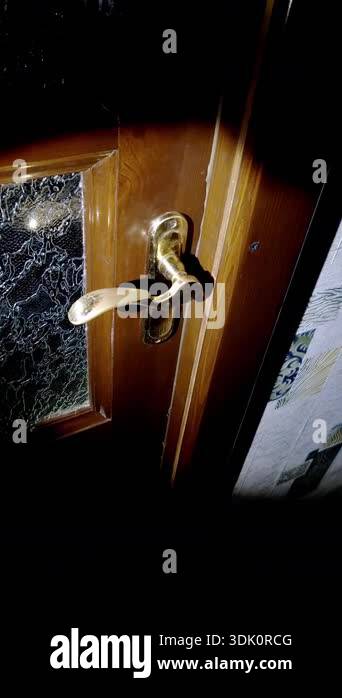 Brass door handle on a wooden door is revealed by a moving light in a ...