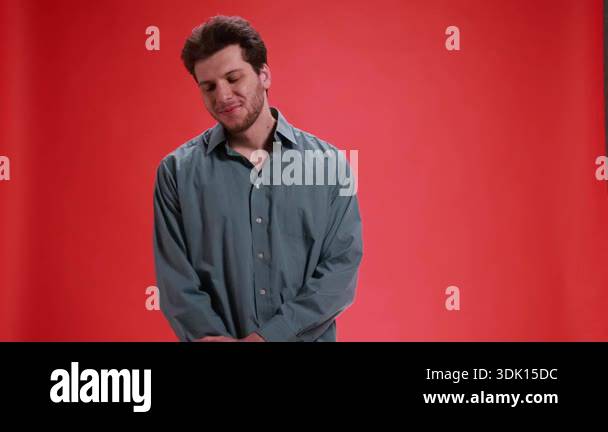 Shy smiling man looking down on red studio background. Concept of ...