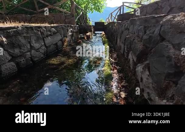 A calm stream flows through a mountain village with stone built banks ...