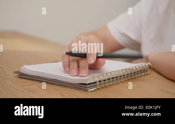 Woman hand tapping pen rhythmically on notebook paper at wooden desk ...
