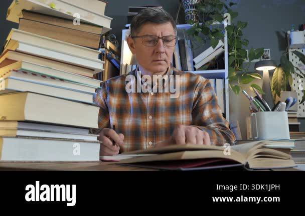 Man studying book at desk with large stack of books in home interior ...