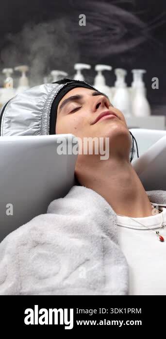 Young man relaxing with his eyes closed at a hair washing station ...