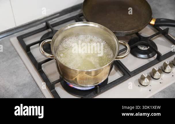 Bubbling clear boiling water inside stainless steel pot heated by blue ...
