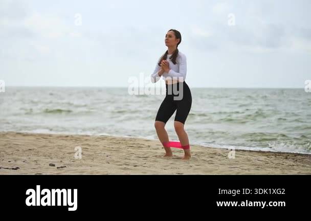 Fit adult woman training with red resistance band around legs, wearing ...