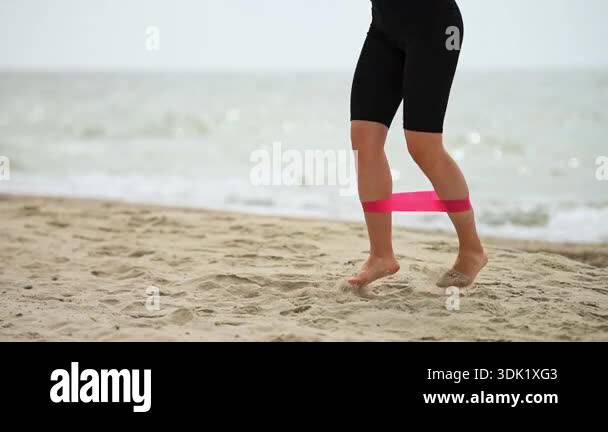 Black high-waisted shorts, pink elastic leg resistance band, sandy ...