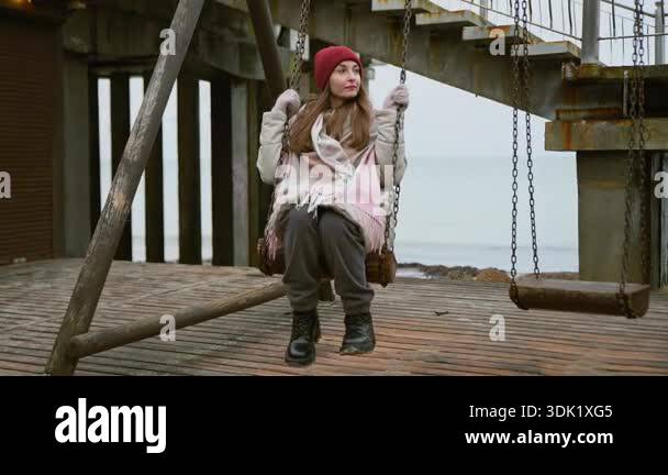 Young woman wearing red beanie and warm clothing swings gently on ...