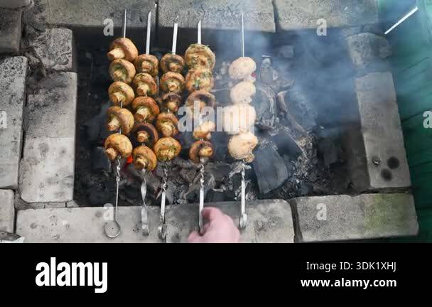 Mushroom kebabs arranged on metal skewers are grilling over hot ...