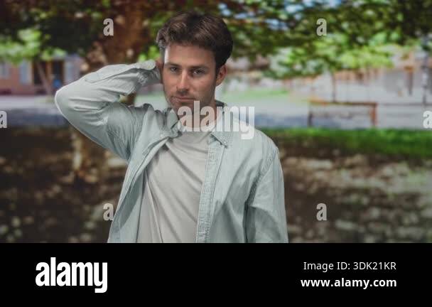 Man touching neck while adjusting a light denim shirt on street under ...