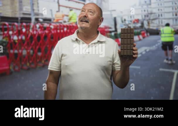 Man holds chocolate bar in hand on street construction site near red ...