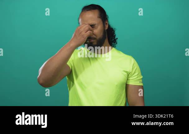 Man pinching bridge of nose in studio with teal backdrop and neon green ...