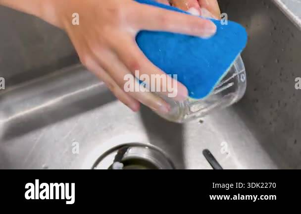 A person uses a blue and yellow sponge to hand wash a blender bowl and ...