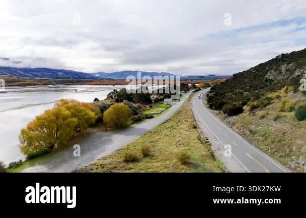 Drone footage glides above a winding lakeside road bordered by autumn ...