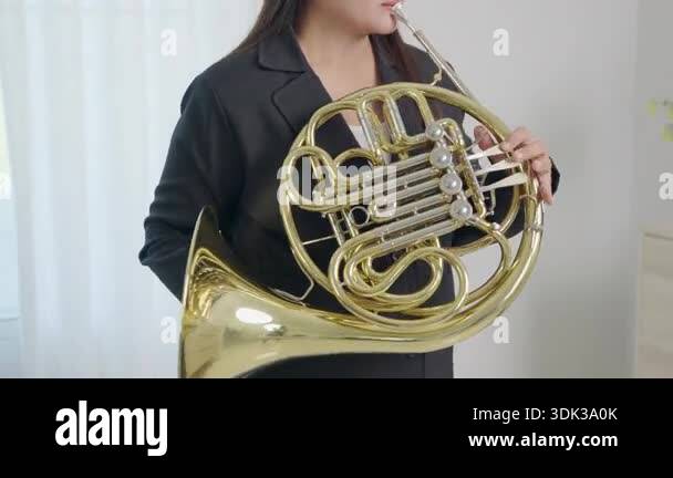 Dressed in a sleek black jacket, a woman skillfully blows a gleaming ...