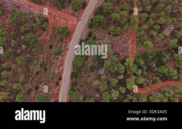 A winding road cuts through a landscape of green trees and red earth in ...
