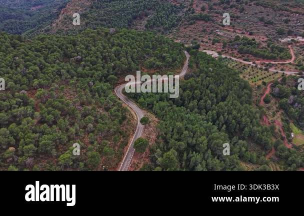 A winding road leads through a dense green forest in rural Spain. The ...