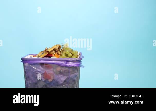 Woman throwing tangerine peels into garbage can on light blue ...