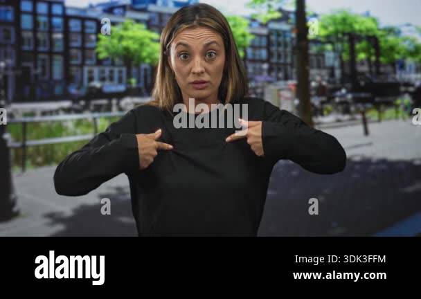 Woman points both fingers to self on street wearing black long sleeve ...