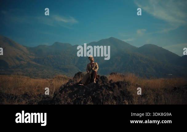 A man in a royal Javanese gold outfit sits calmly on a pile of volcanic ...