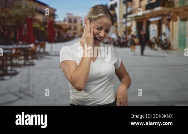 Young woman wincing while holding cheek with hand on busy city street ...