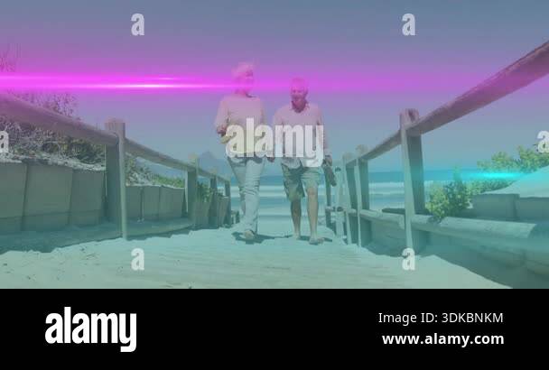 Senior couple stepping onto ramp, walking hand in hand toward ocean ...