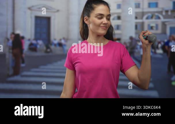 Young hispanic woman lifts a grey dumbbell while flexing her arm on a ...