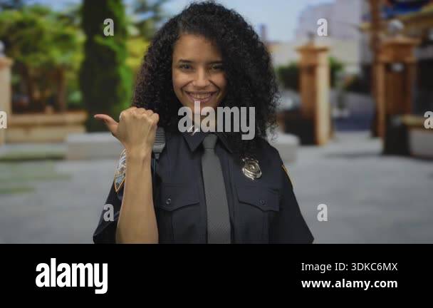 Female officer smiling confidently in uniform on a sunny street points ...