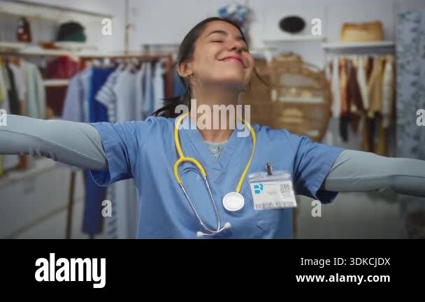 Woman wearing stethoscope in blue medical uniform opens arms to camera ...
