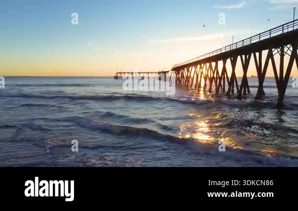 Calm waves rolling onto the shore with a long wooden pier during a ...