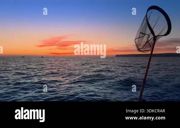 Fishing landing net on boat at sunset, orange sky over calm ...