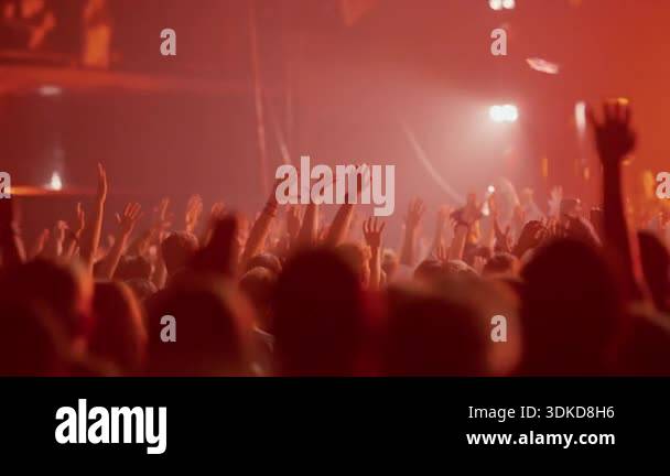 A large, energetic crowd with hands raised in the air, dancing and ...