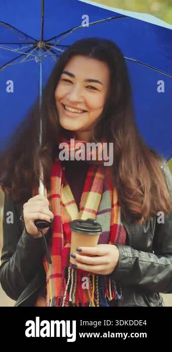 Young woman with blue umbrella wearing leather jacket with checkered ...