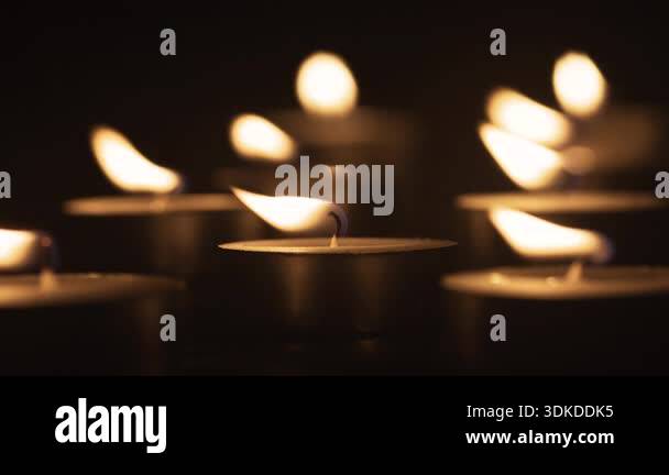 Close up of burning candles with warm yellow flames glowing in darkness ...