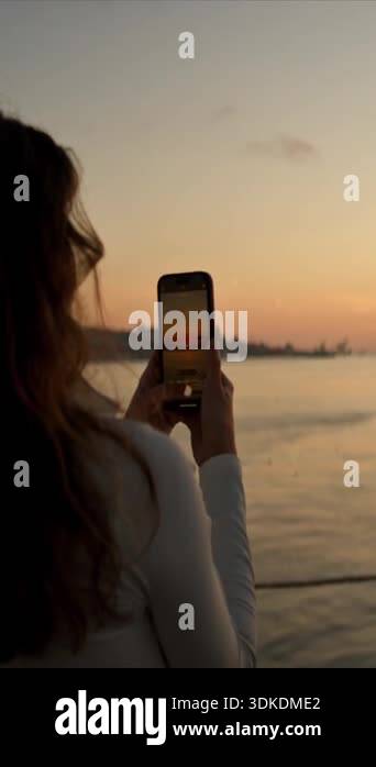Tourist taking pictures of beautiful orange sunset over ocean with ...