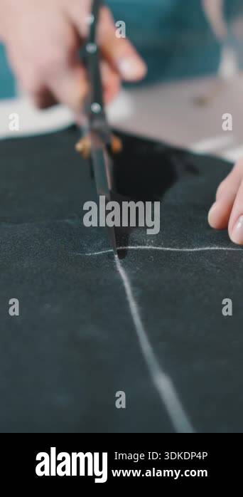 A woman is cutting fabric with scissors. The scissors are on a table ...