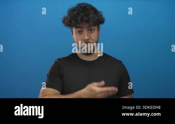 Young man with beard makes gestures against a blue background ...