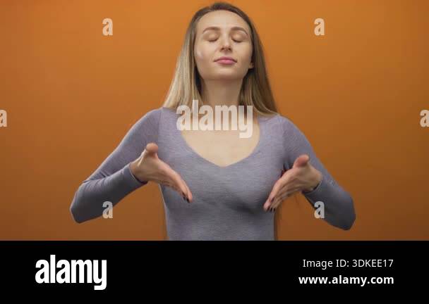 Woman meditating with eyes closed against vibrant orange background ...