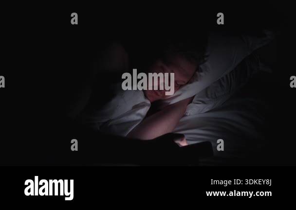 Sleepless man scrolling on his phone in a dark room, suffering from ...