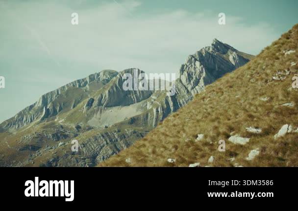 Rugged karst limestone peaks rise behind a steep tussock slope. A slow ...