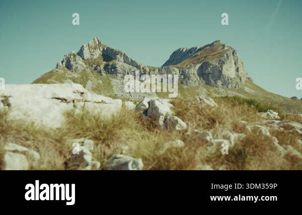 Limestone ridge with twin peaks and a cliff band rises above dry grass ...