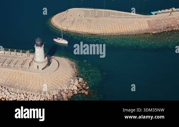 Aerial daytime scene shows a curved breakwater, a white lighthouse with ...